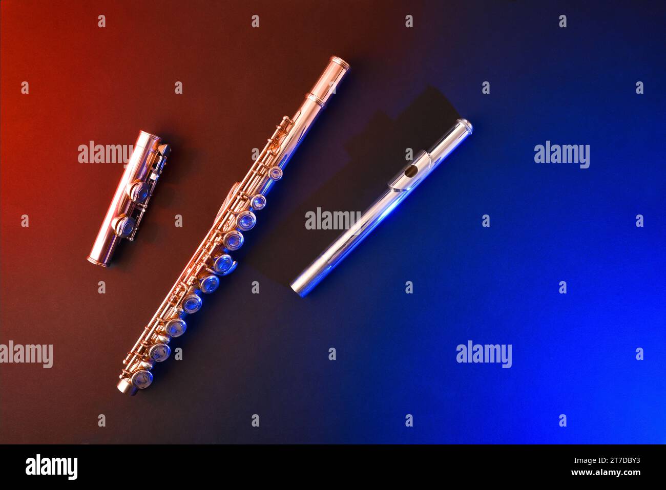 Disassembled metal flute isolated on dark table illuminated with red ...
