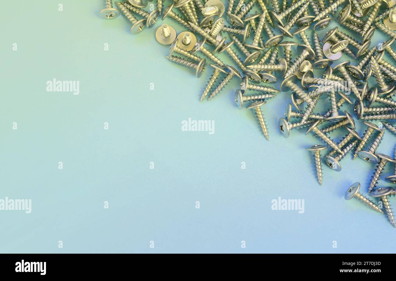 A lot of small silver screws lies on a light blue background. Minimal ...