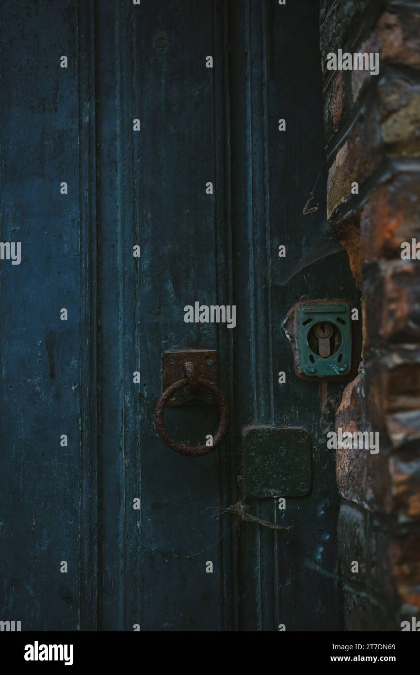 A weathered old blue wooden front door with a rusty round knocker and ...