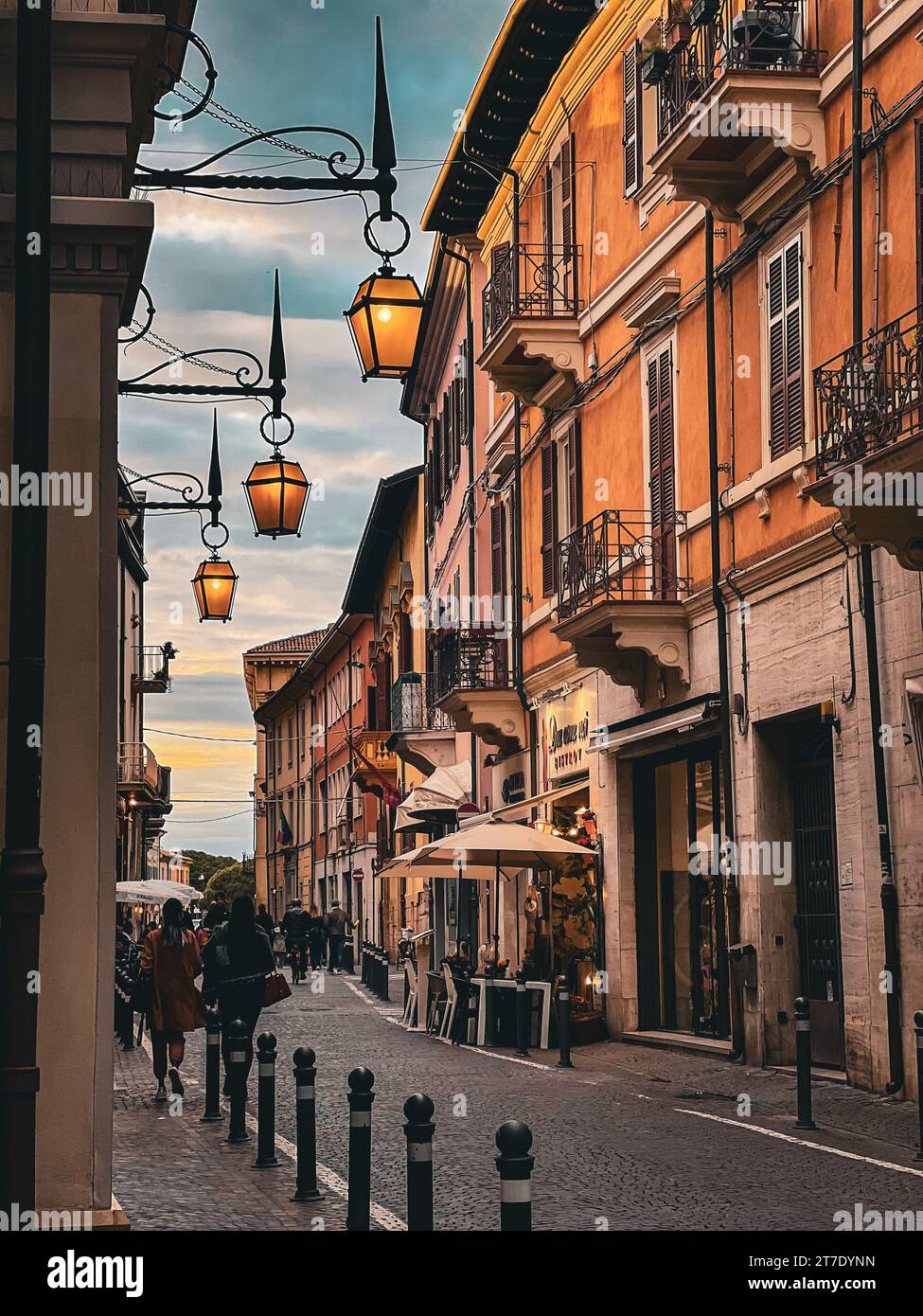 A narrow urban street illuminated by a series of streetlamps surrounded ...