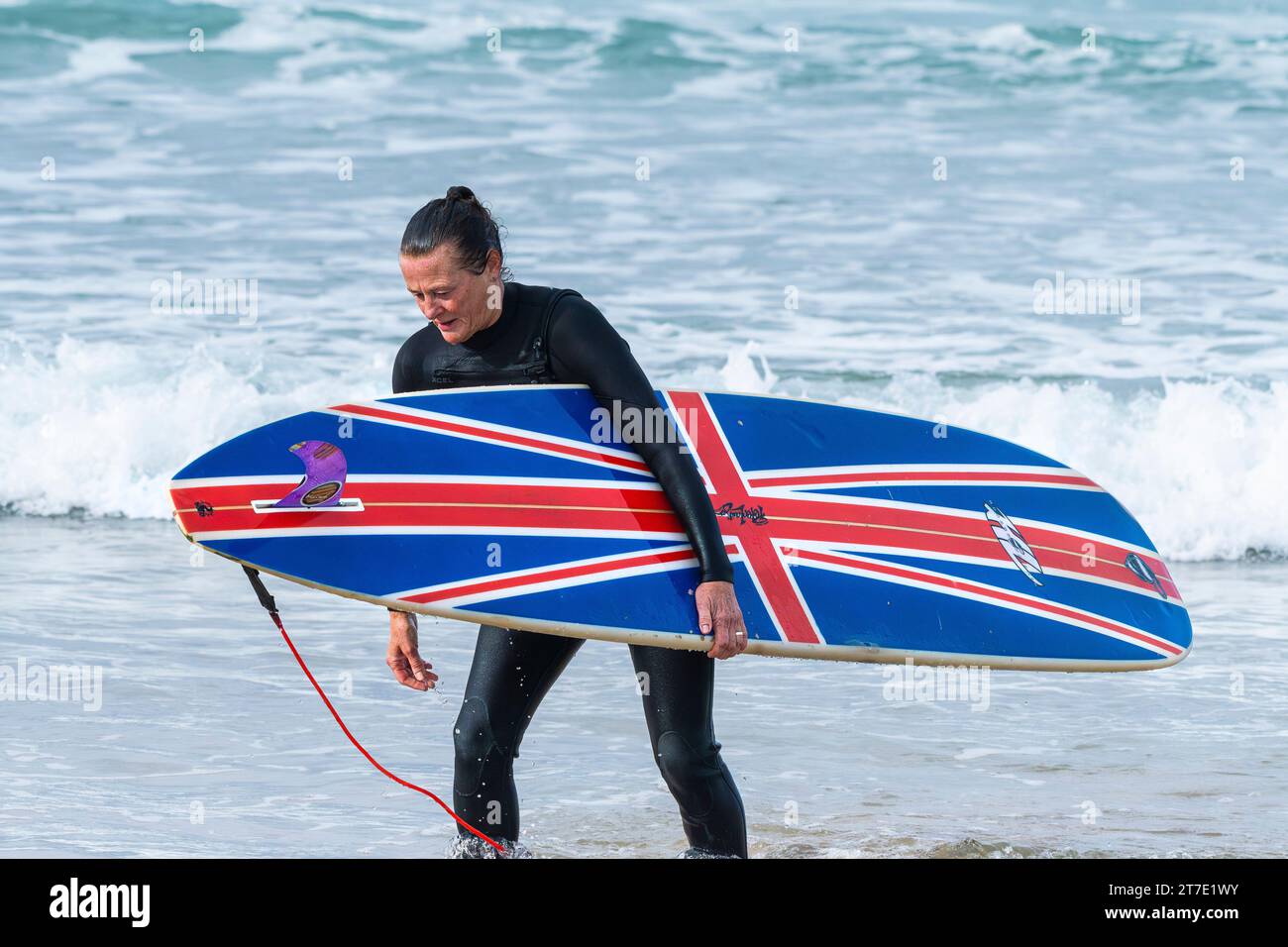 A tired surfer carrying a distinctive surfboard after a surfing session ...
