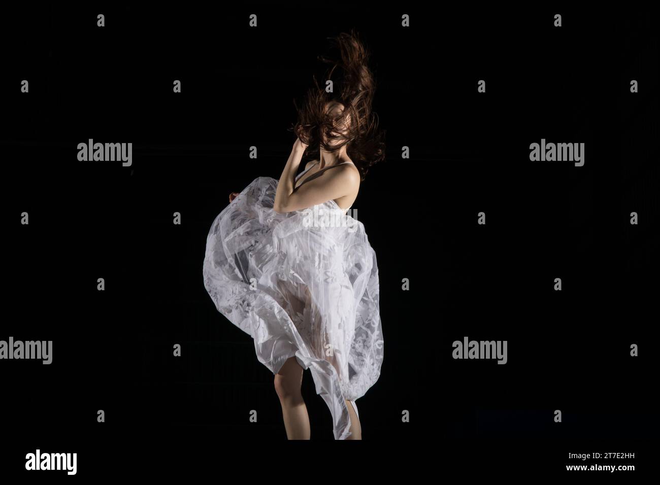 A female with dark hair obscuring her face in front of a solid black ...