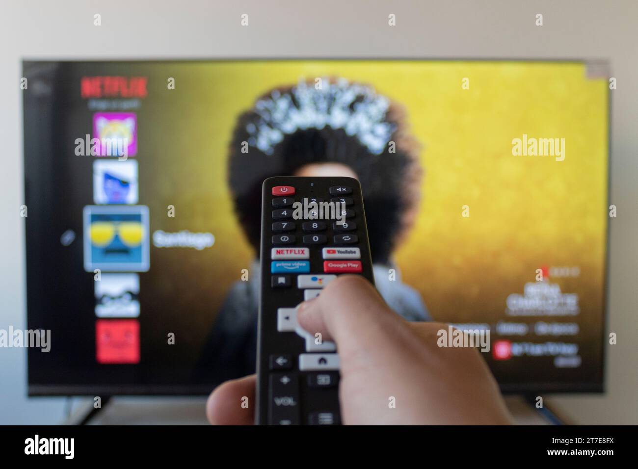 A male hand holding a smart tv remote control with blurred netflix ...