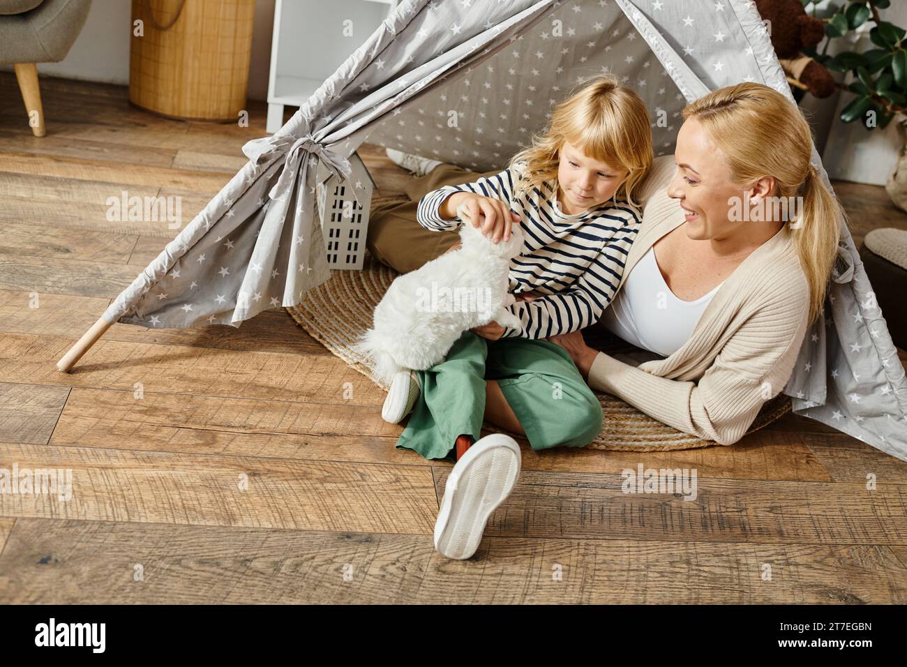 happy girl with prosthetic leg playing with soft toy rabbit near mother ...