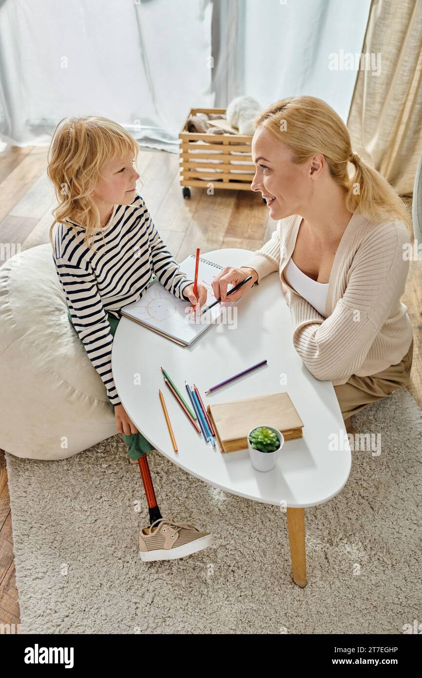 happy mother and kid with prosthetic leg drawing on paper with colorful ...