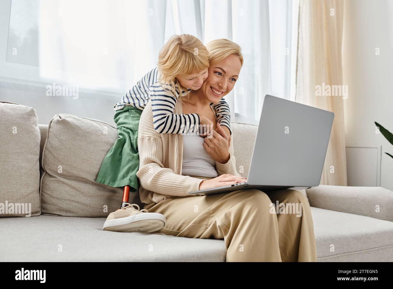 happy kid with prosthetic leg hugging blonde mother working on laptop ...