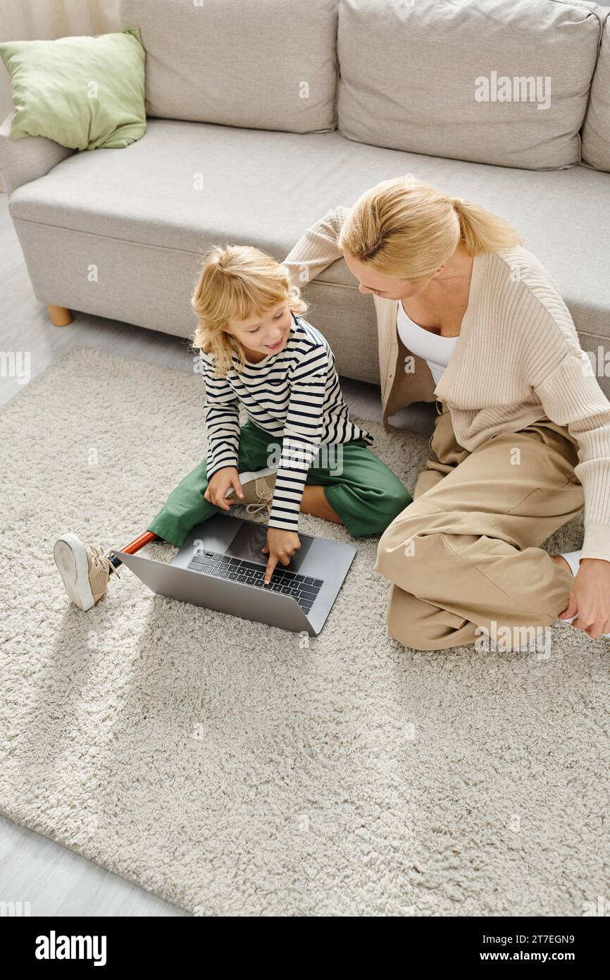 happy child with prosthetic leg pointing at laptop and sitting on ...