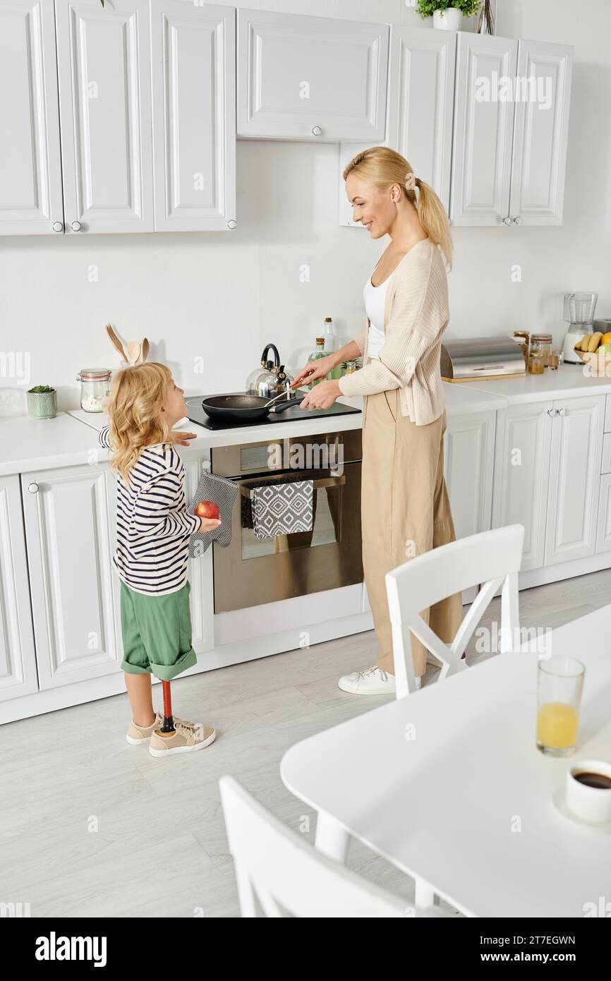 cute girl with prosthetic leg holding plate and helping happy mother washing dishes in kitchen ...