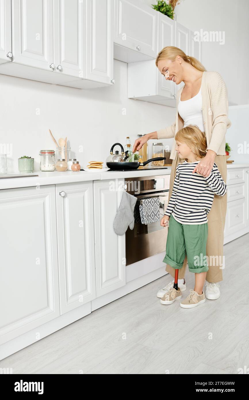 joyful mother cooking and holding hand of disabled little daughter with ...