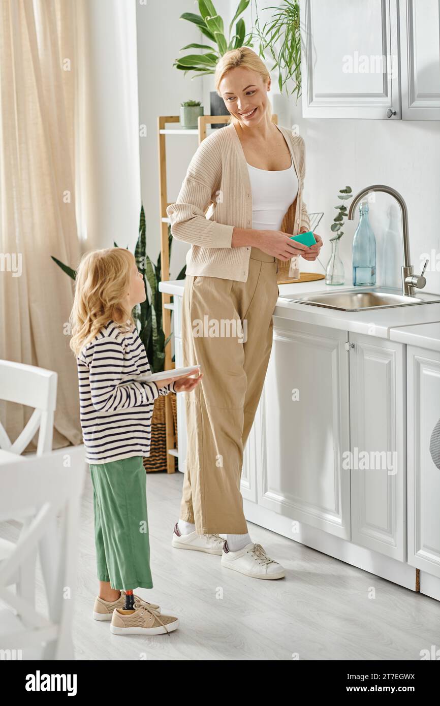 little girl with prosthetic leg holding plate and helping happy mother ...