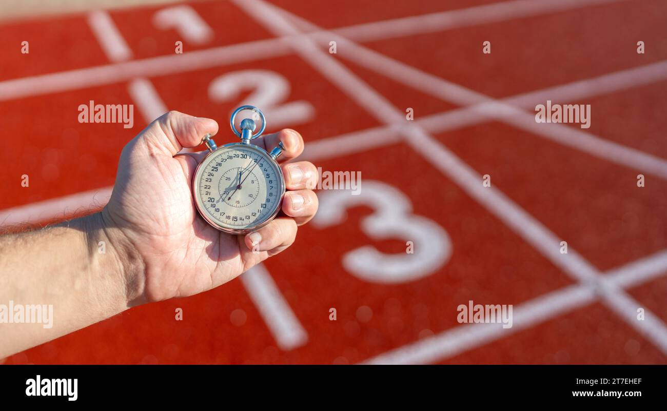 Hand holding a stopwatch on a red running track, numbers on lanes ...