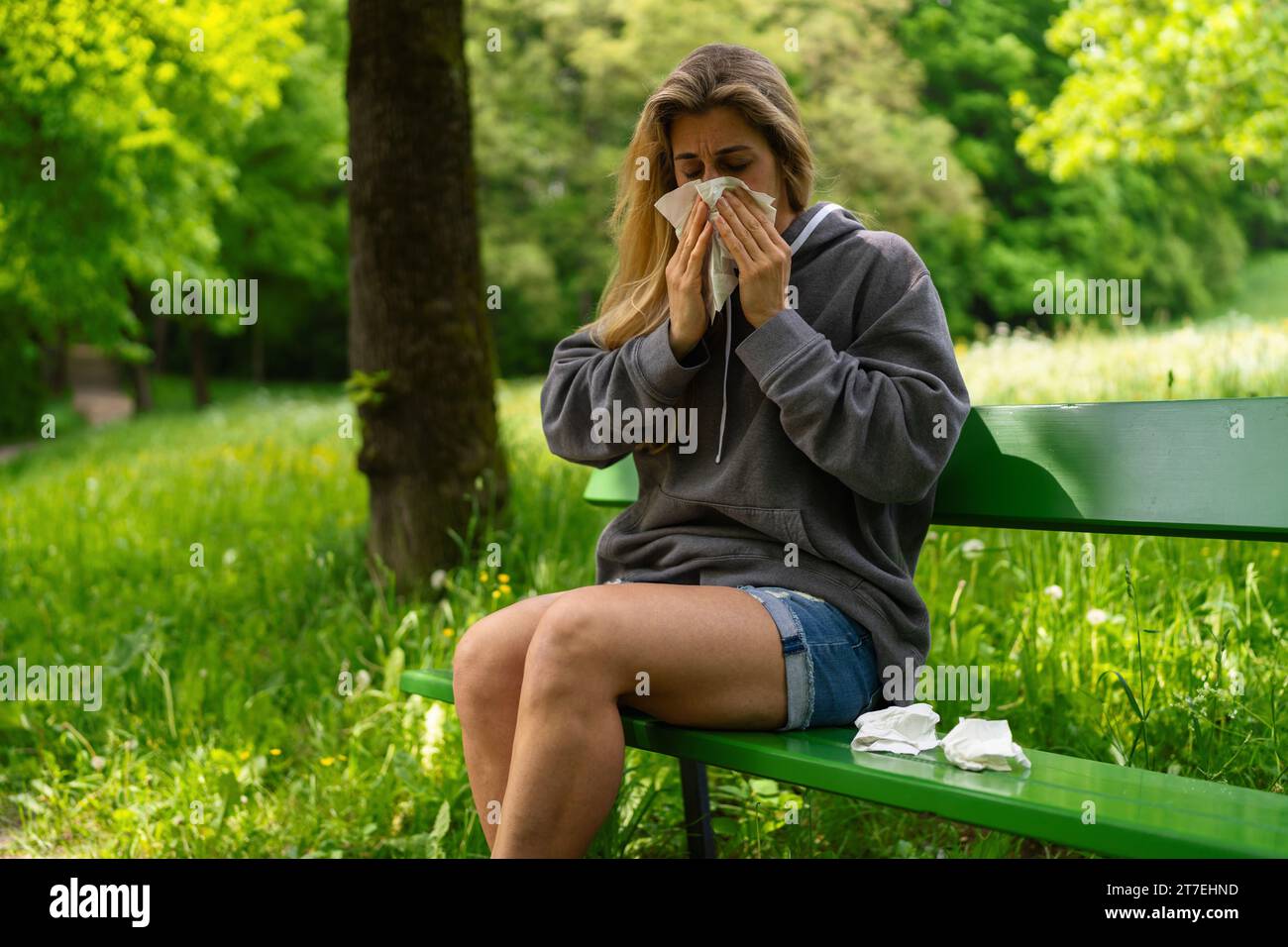 Woman sneezing on a green park bench, used tissues beside, because of ...