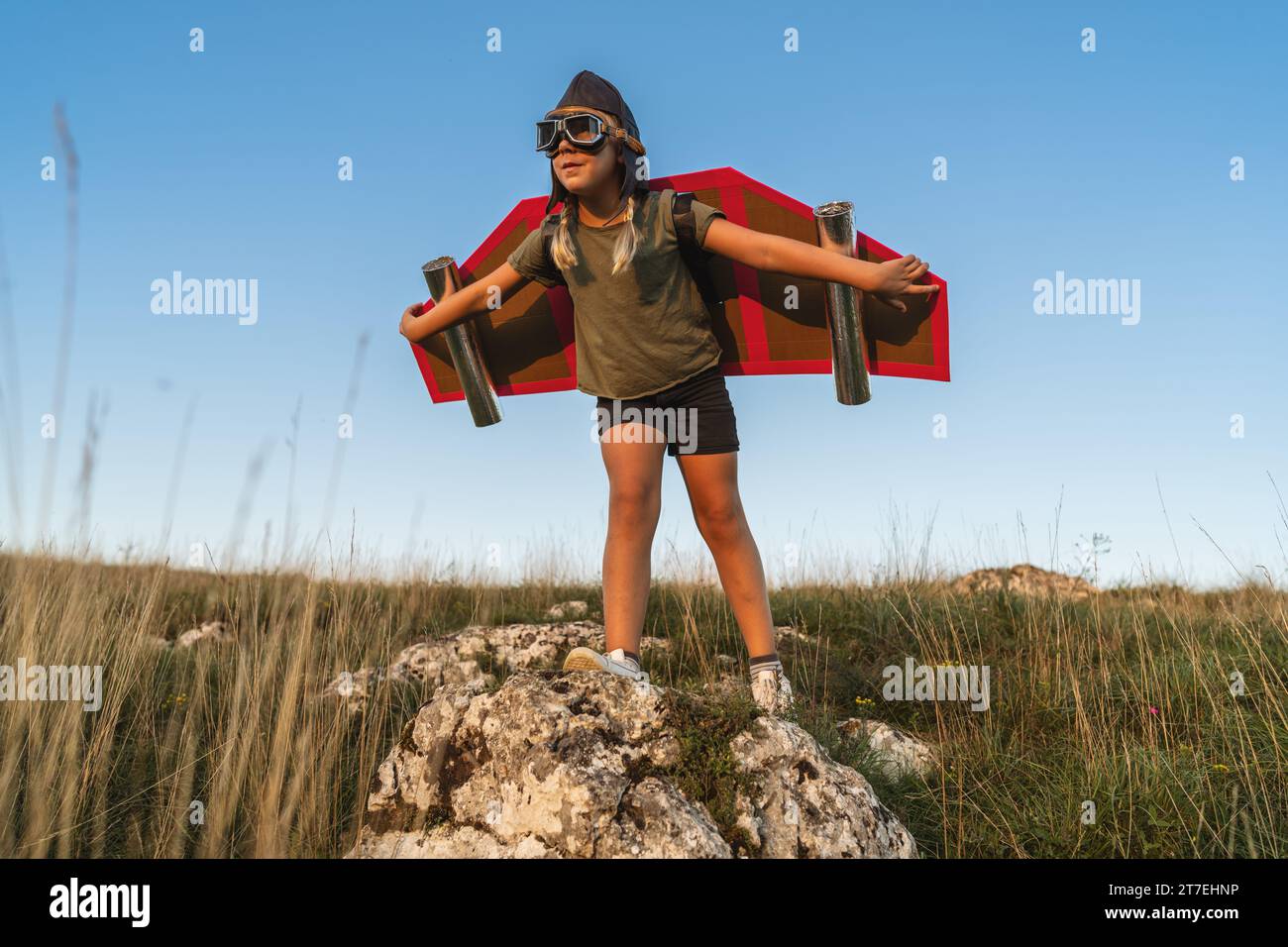 Young child with cardboard jetpack and wings standing on a rock ...