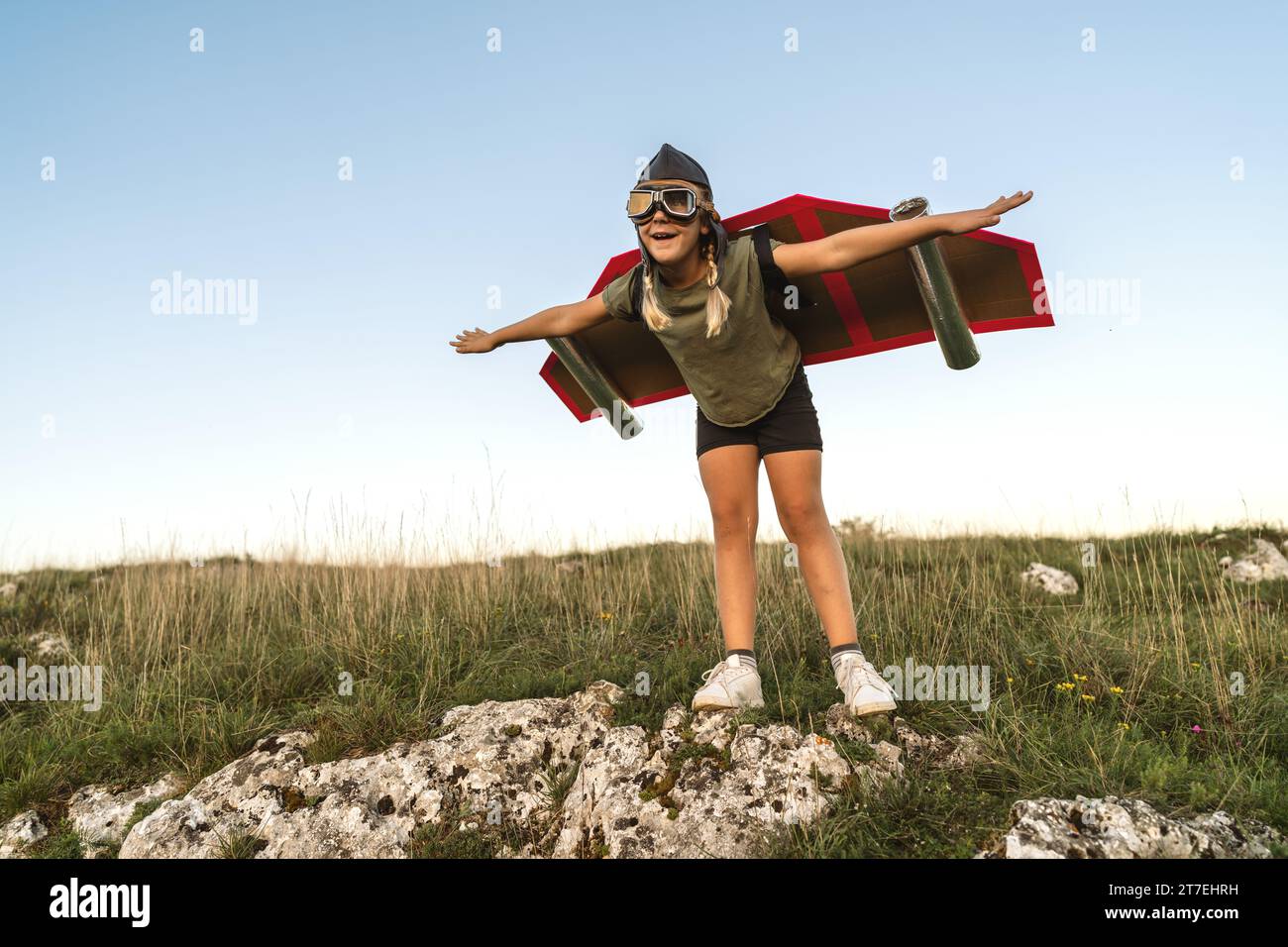 Joyful child with arms outstretched wearing cardboard wings and helmet ...