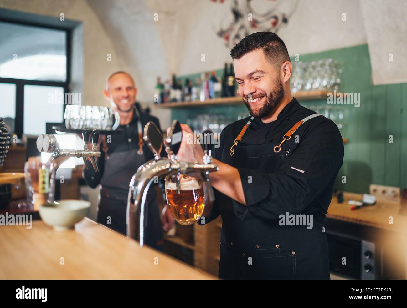 Stylish bearded barman dressed black uniform smiling at camera, beer ...