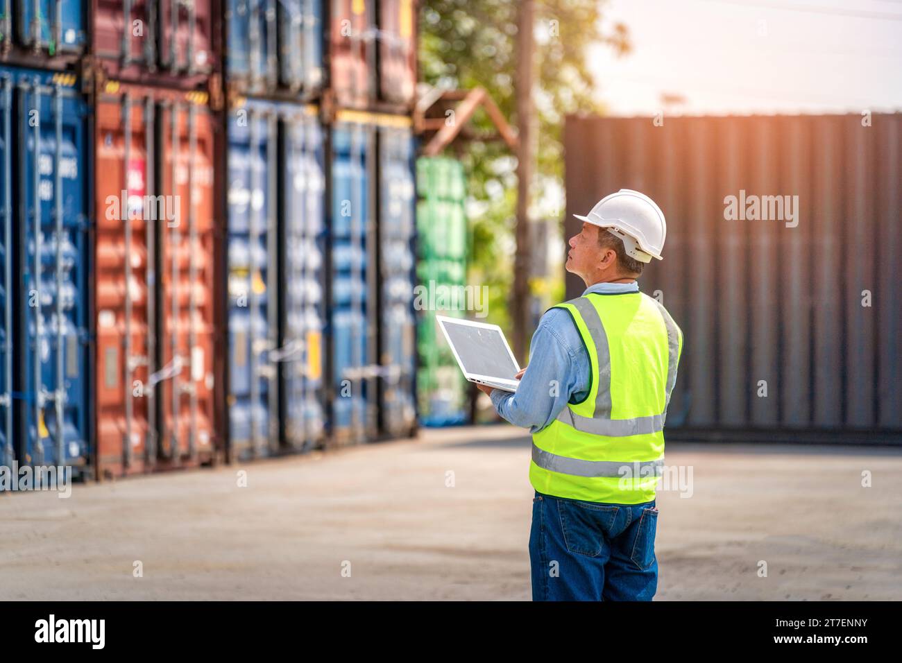 Engineer or foreman holding laptop and wears PPE checking container ...