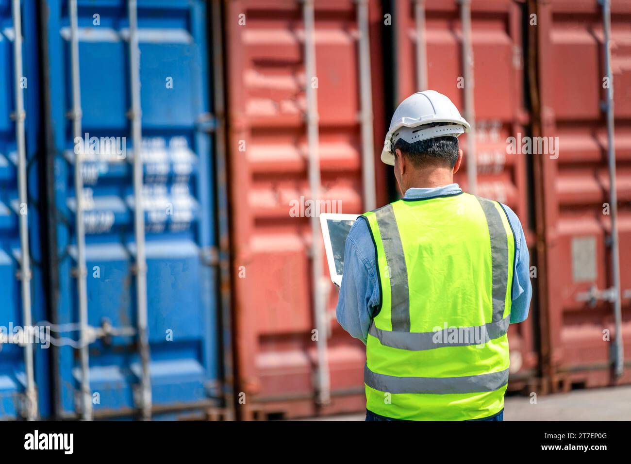 Engineer or foreman holding laptop and wears PPE checking container ...