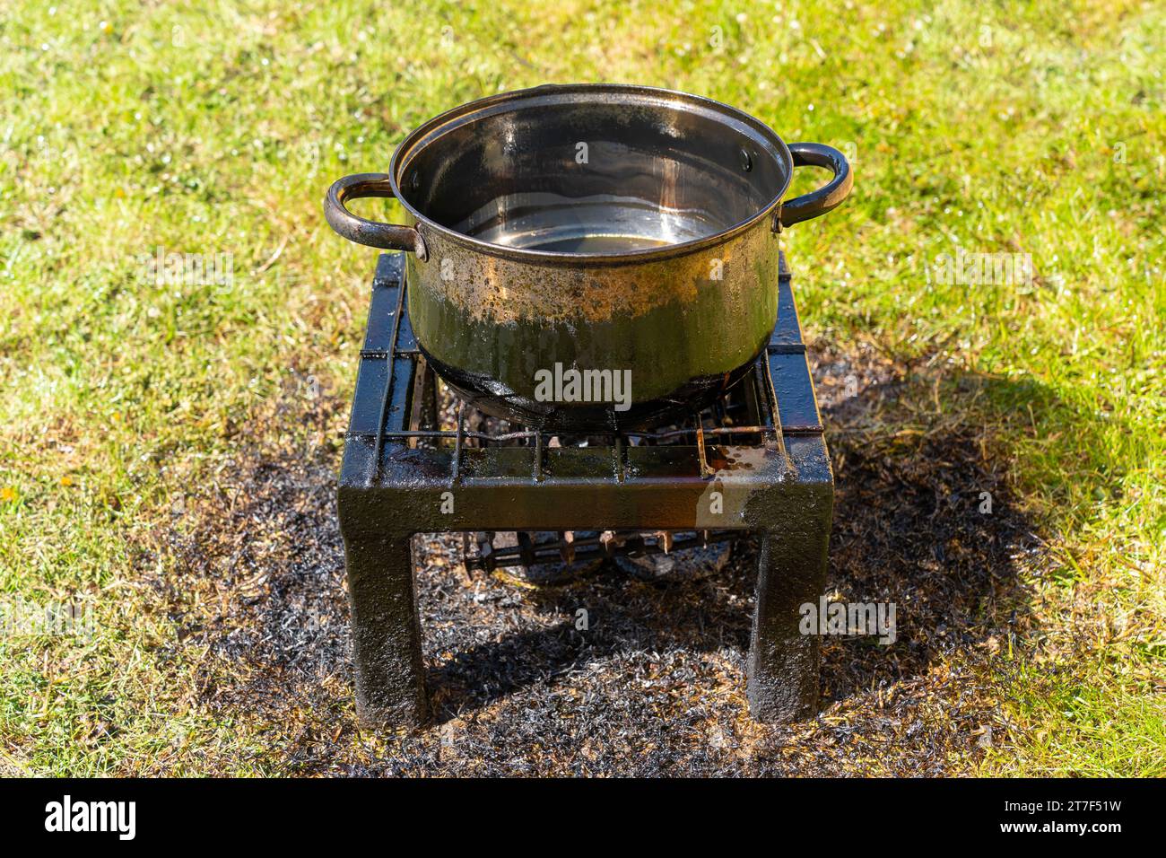 Burnt sooty pot and stove outdoors with green grass in the background ...