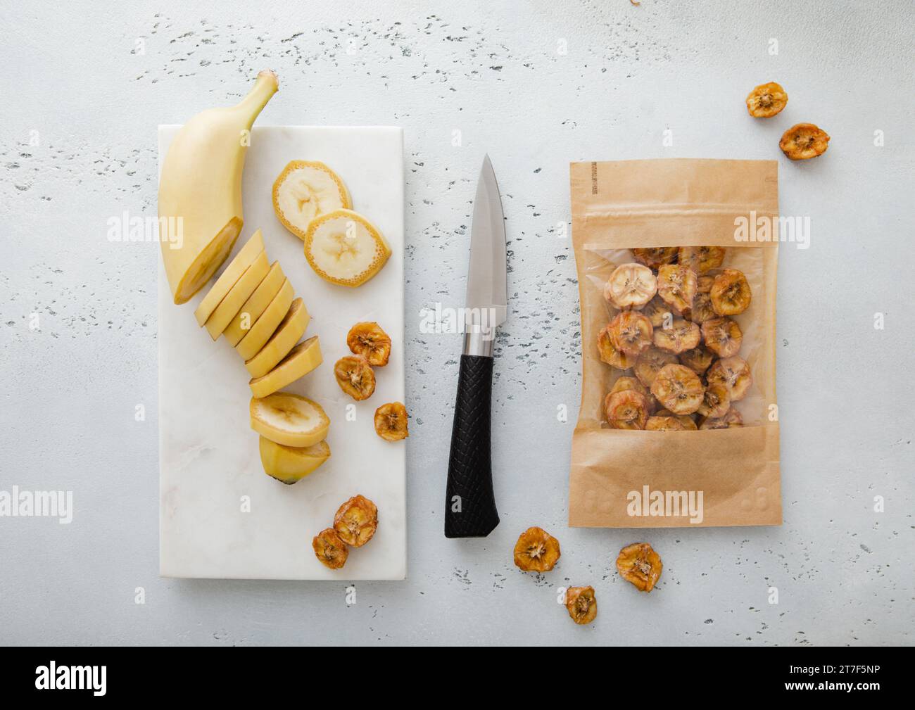Pack of dried bio banana chip slices with knife and raw banana.Top view ...