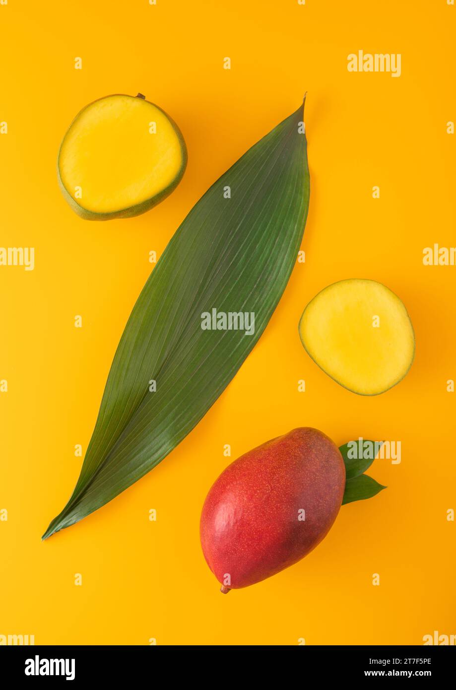 Fresh red mango and two halves and large leaf on yellow background.Top ...