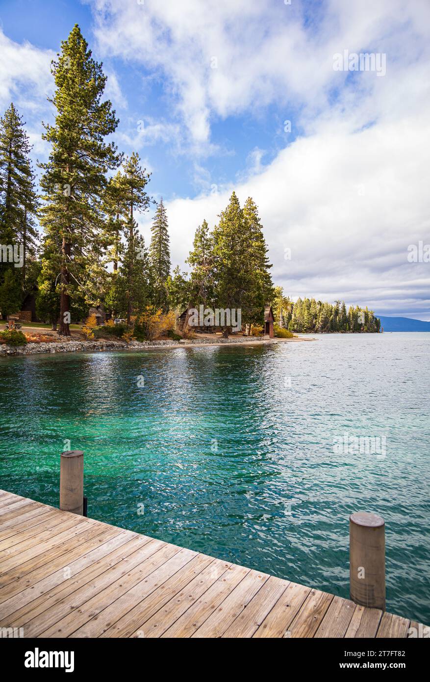 Clear blue-green lake water with a dock and pine trees on a sunny day ...