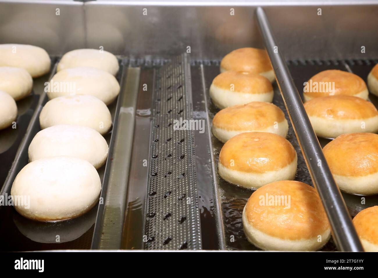 doughnuts being cooked on both sides with coking oil on the factory ...