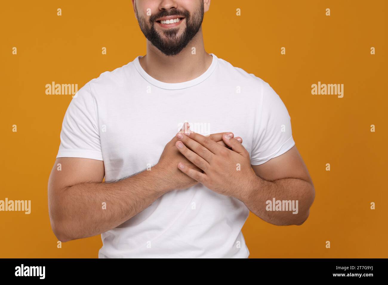 Thank you gesture. Grateful man holding hands near heart on orange ...