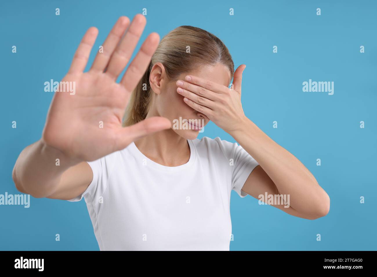 Embarrassed woman covering face on light blue background Stock Photo ...
