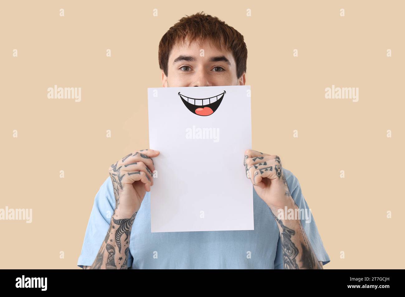 Young tattooed man with paper smile on beige background Stock Photo - Alamy