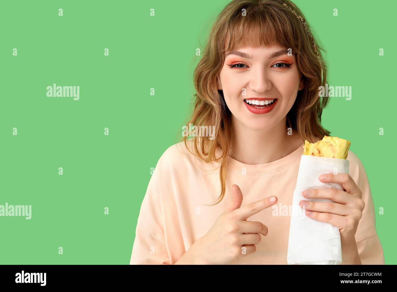 Young woman pointing at tasty sandwich wrap on green background ...