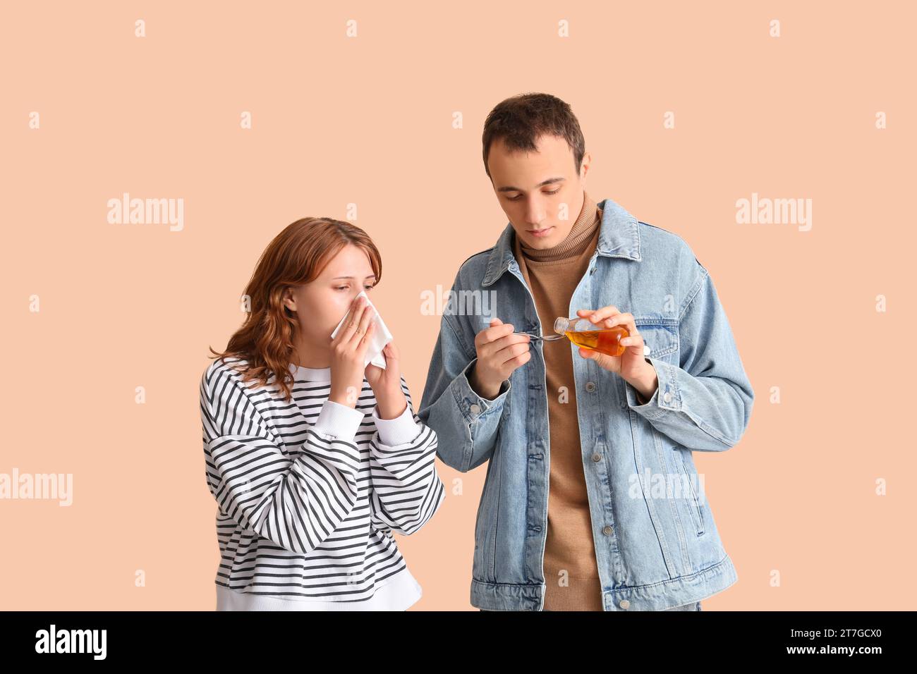 Young man giving his ill girlfriend cough syrup on beige background ...