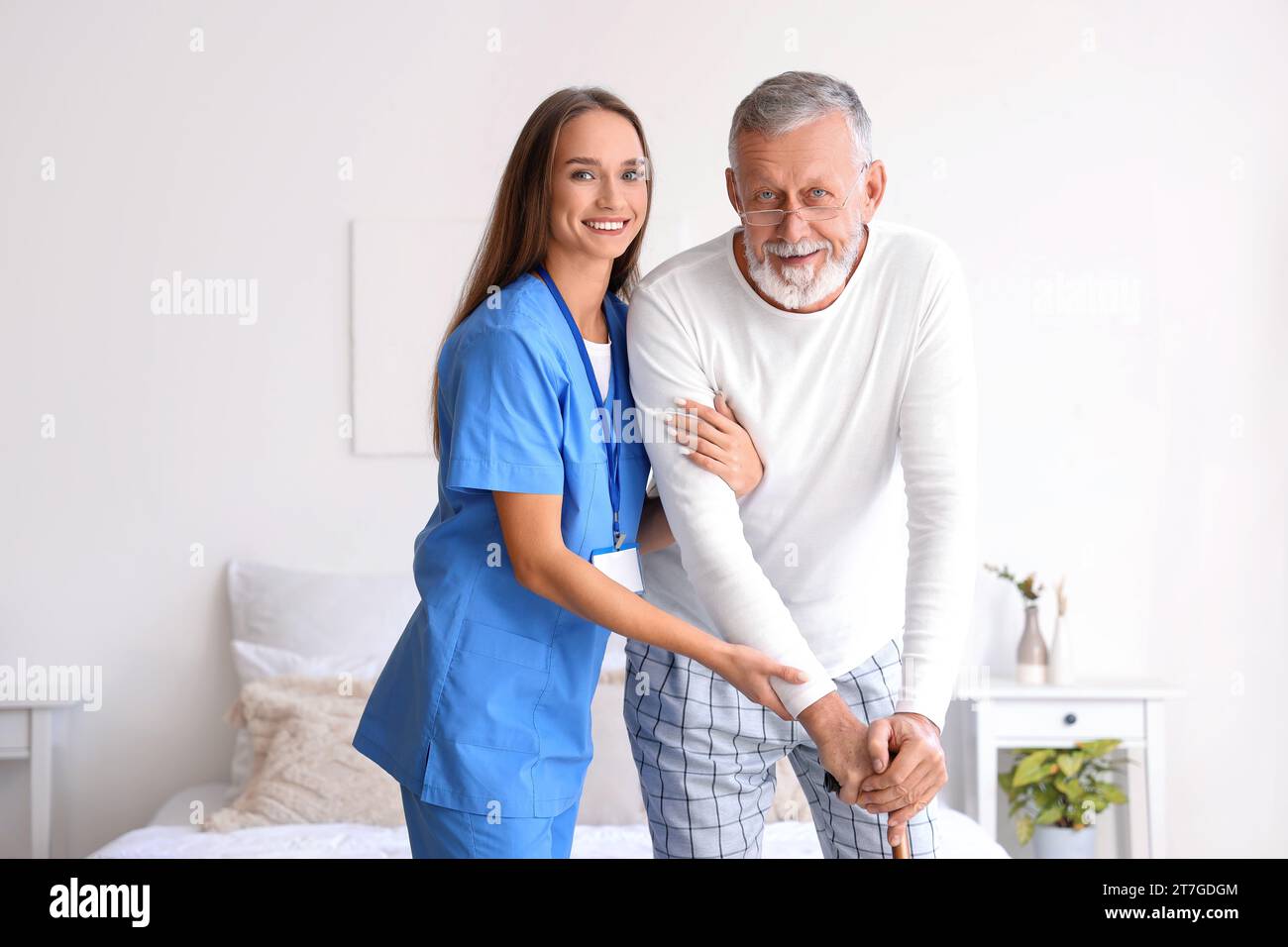 Female caregiver helping senior man with walking stick in bedroom Stock ...