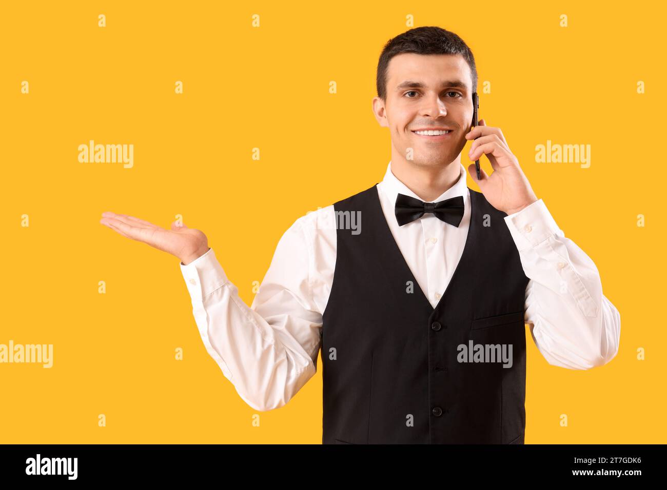 Male waiter with mobile phone showing something on yellow background ...