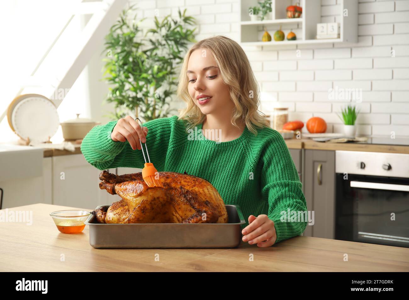 Beautiful young woman preparing tasty baked turkey at table in kitchen ...