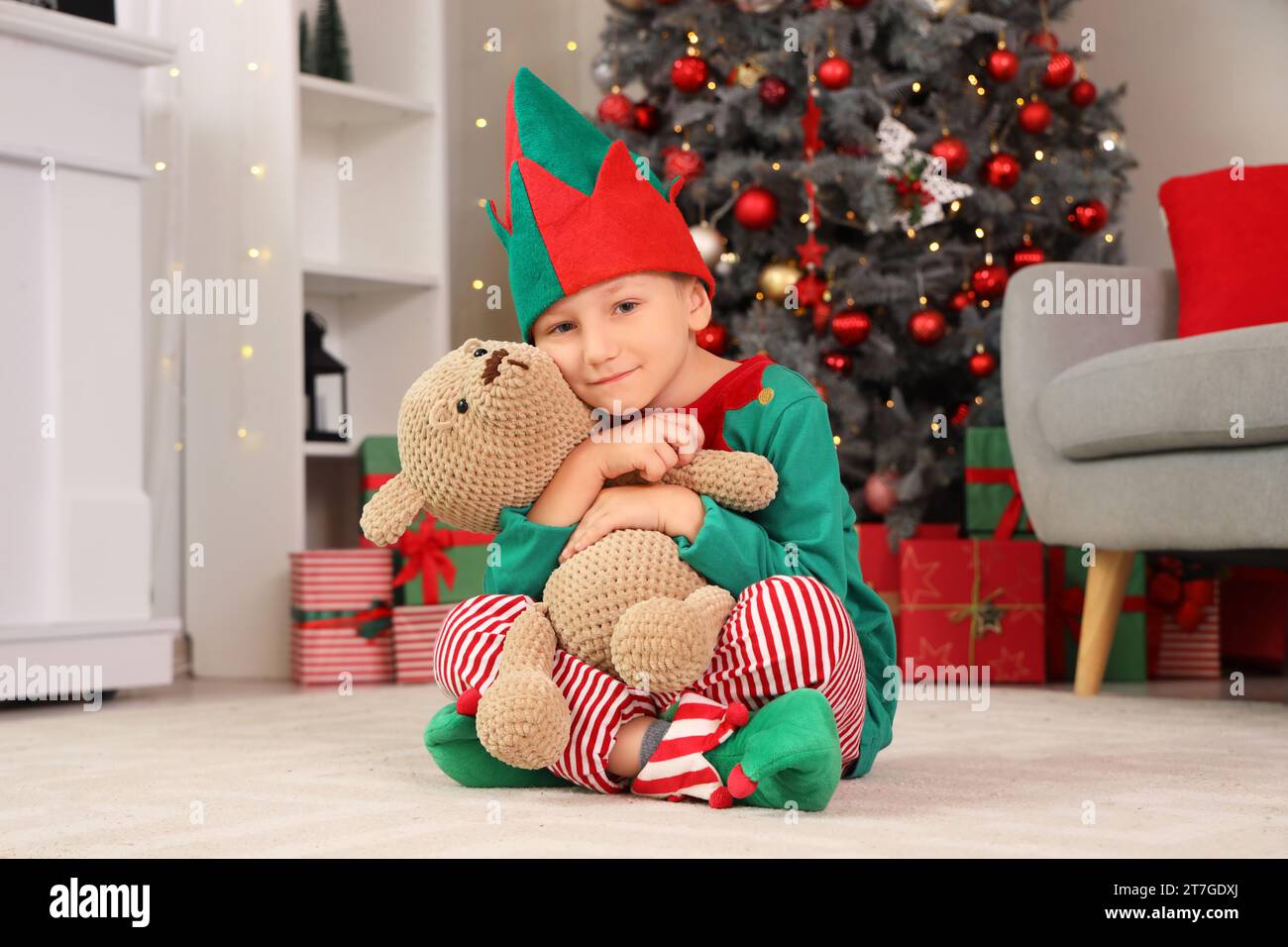 Cute little boy in elf costume with toy bear at home on Christmas eve ...