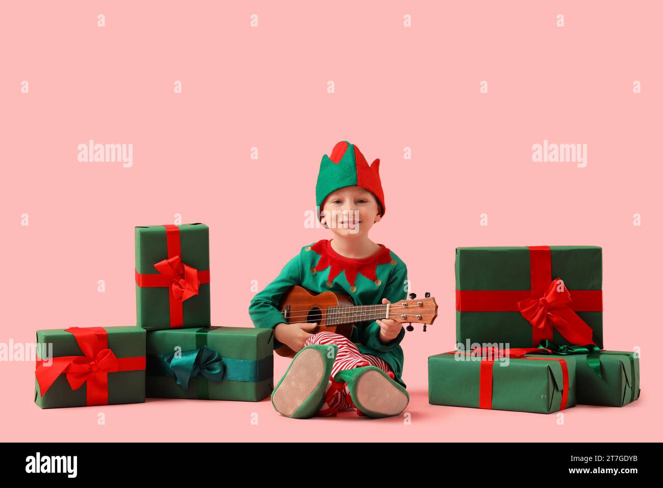 Cute little elf with Christmas gifts playing guitar on pink background ...