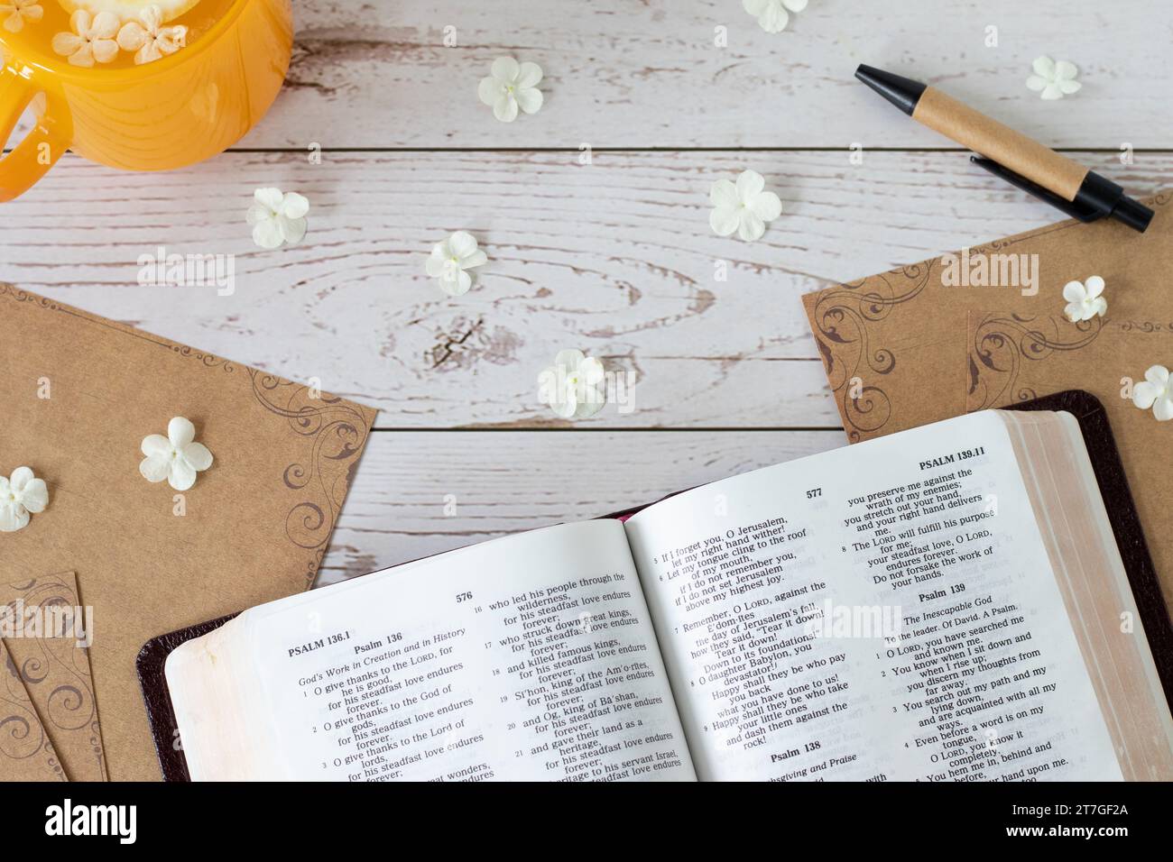Open holy bible book with a cup of tea, old paper, pen, and white flowers on wooden table. Top ...