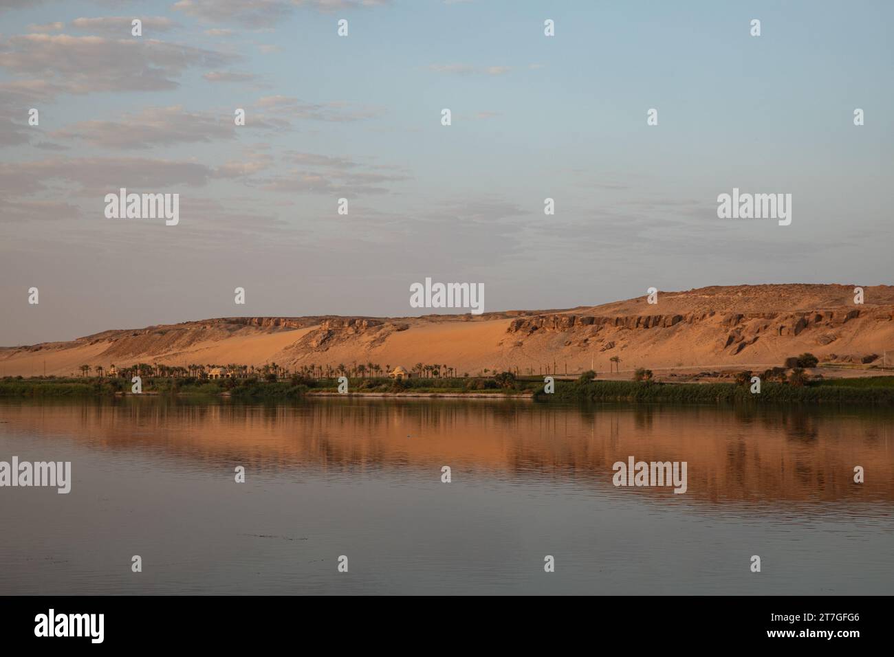 Red sandstone hills and sand dunes rise above oasis on the banks for ...