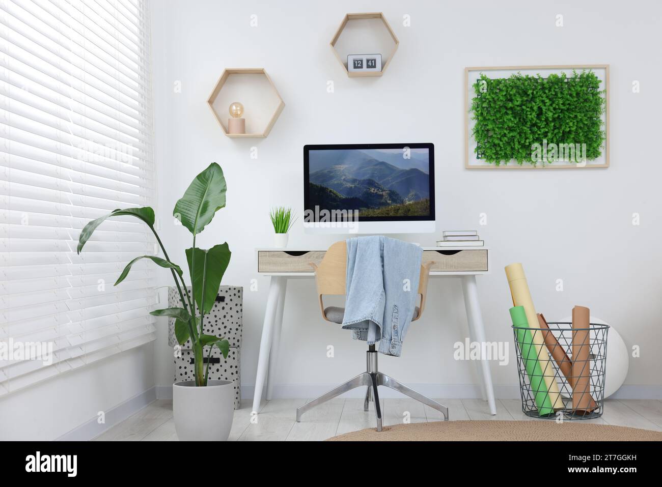 Green artificial plant wall panel and desk with computer in light room ...
