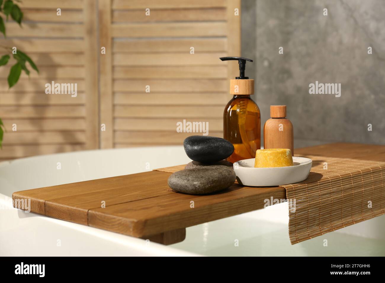 Wooden tray with spa products and stones on bath tub in bathroom. Space ...