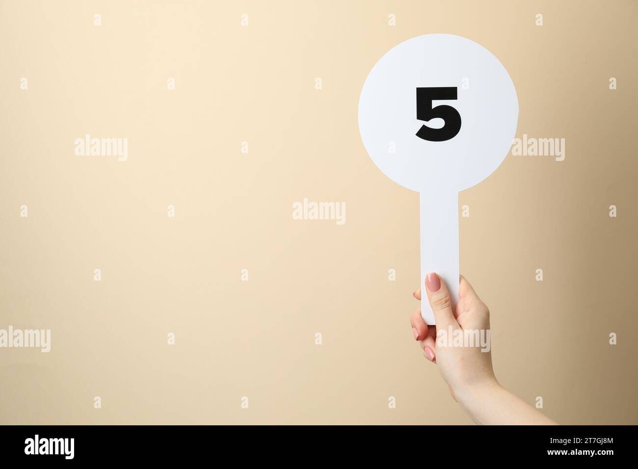 Woman holding auction paddle with number 5 on beige background, closeup ...