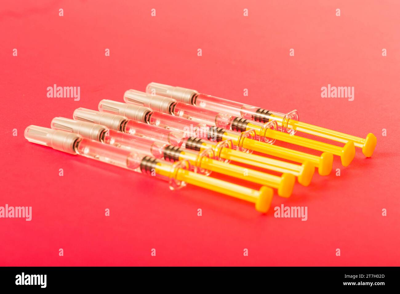 Row yellow transparent syringe red background Stock Photo - Alamy