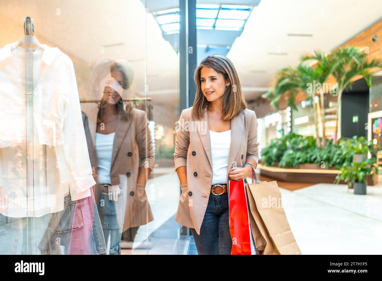 Woman looking at clothes through the window of a shop while walking ...