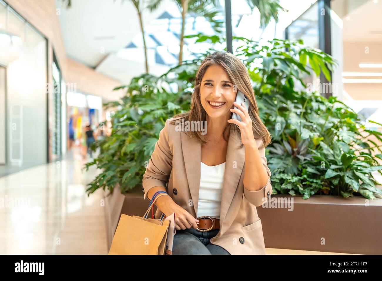 Happy woman shopping and talking to the mobile sitting on a bench in a ...