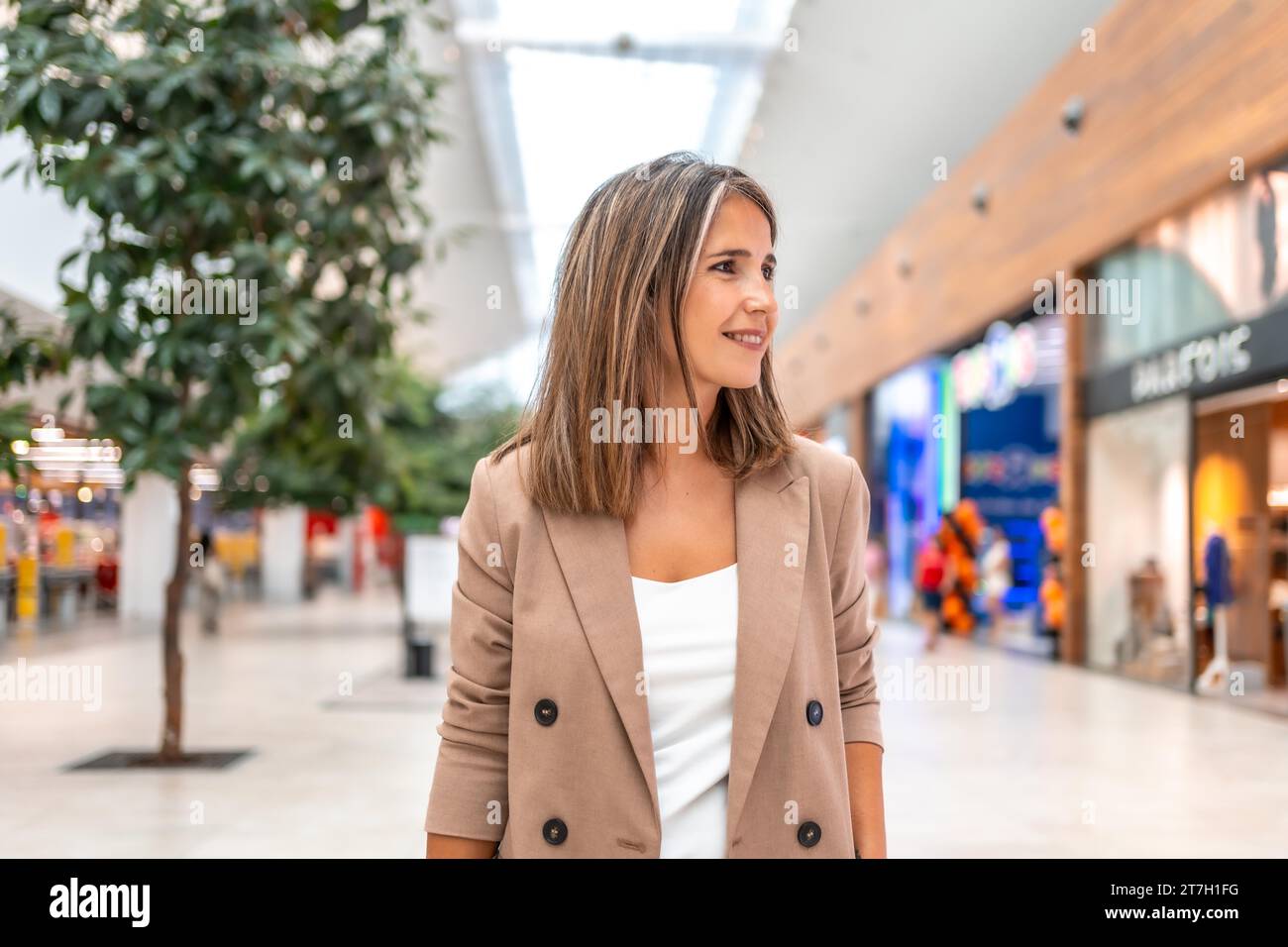 Woman walking along a indoor shopping mall with trees and shops inside ...