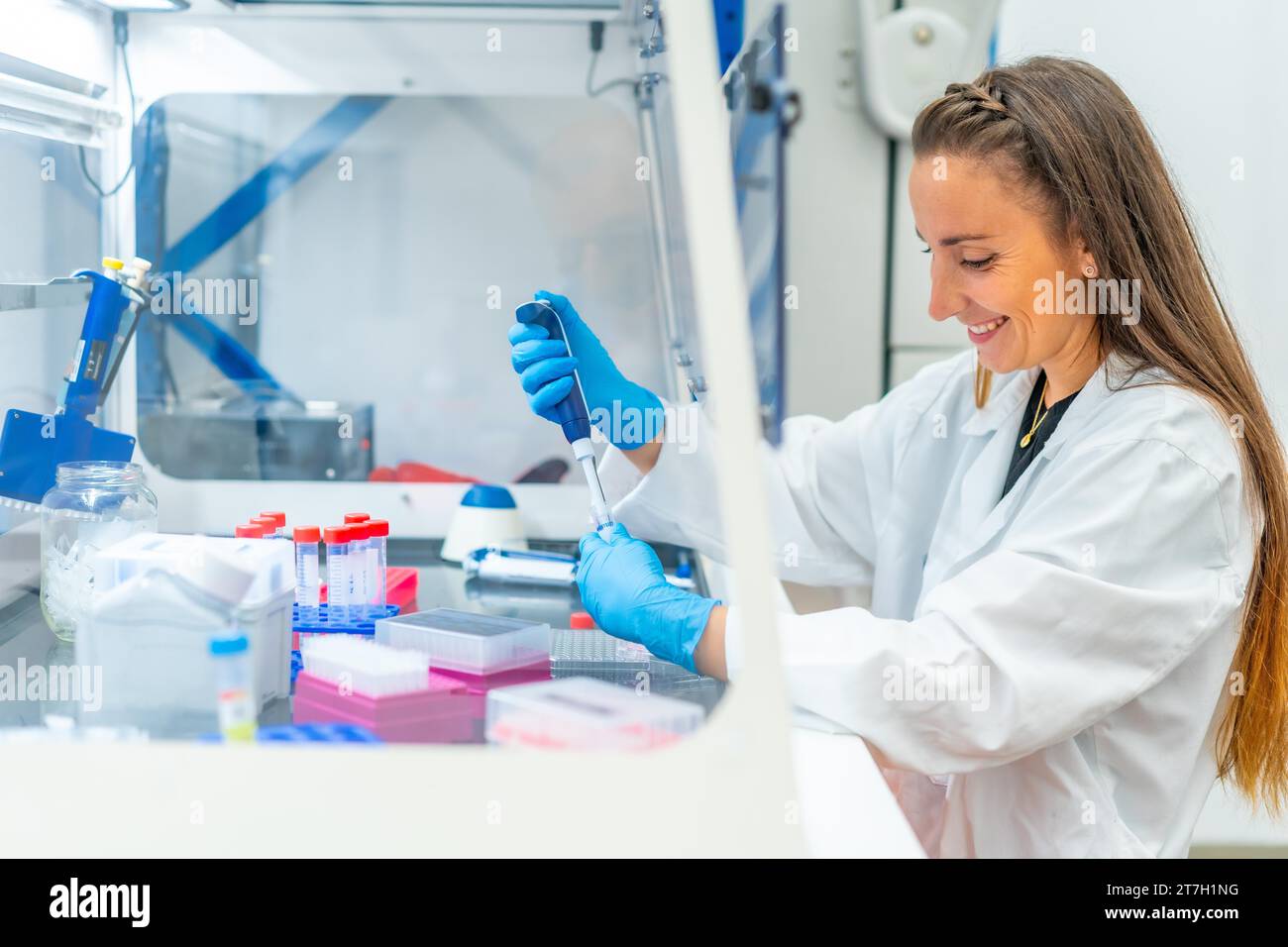 Smiling biologist using pipette to extract cells from a tray in a ...