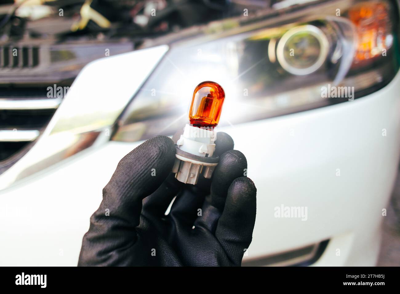 Orange turn signal light bulb in auto mechanic hand with a car blurred ...