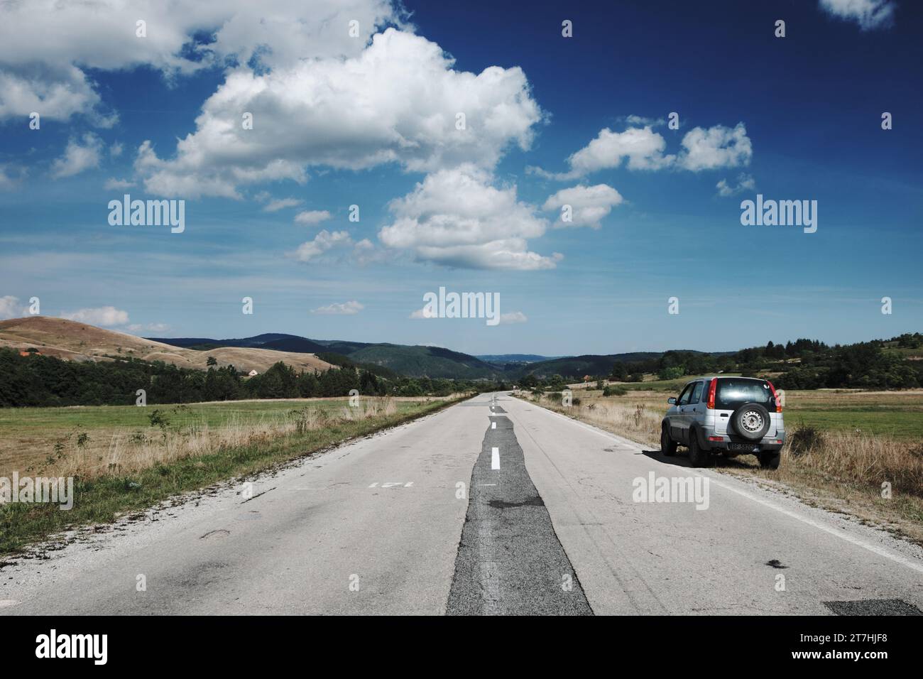 roadside car on rural road trip landscape below white clouds in blue ...