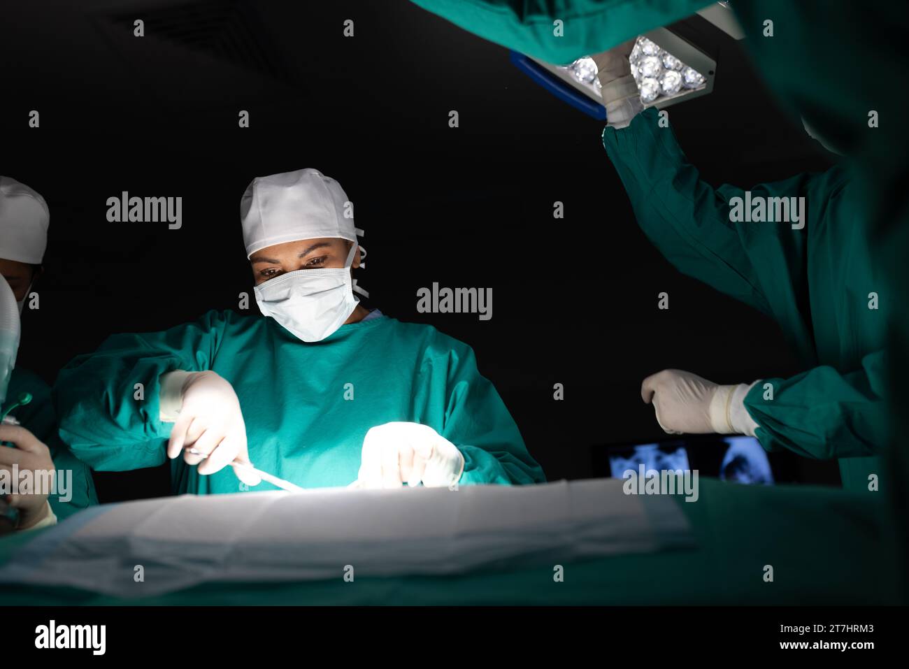 Diverse surgeons wearing surgical gowns operating on patient in ...