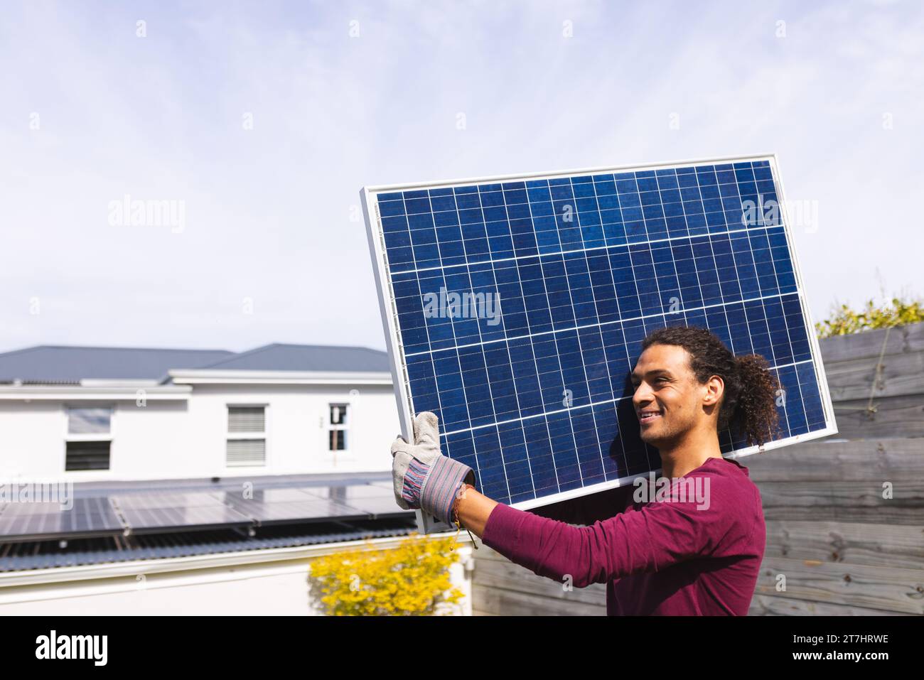 Happy biracial man carrying solar panel and smiling in sunny garden ...